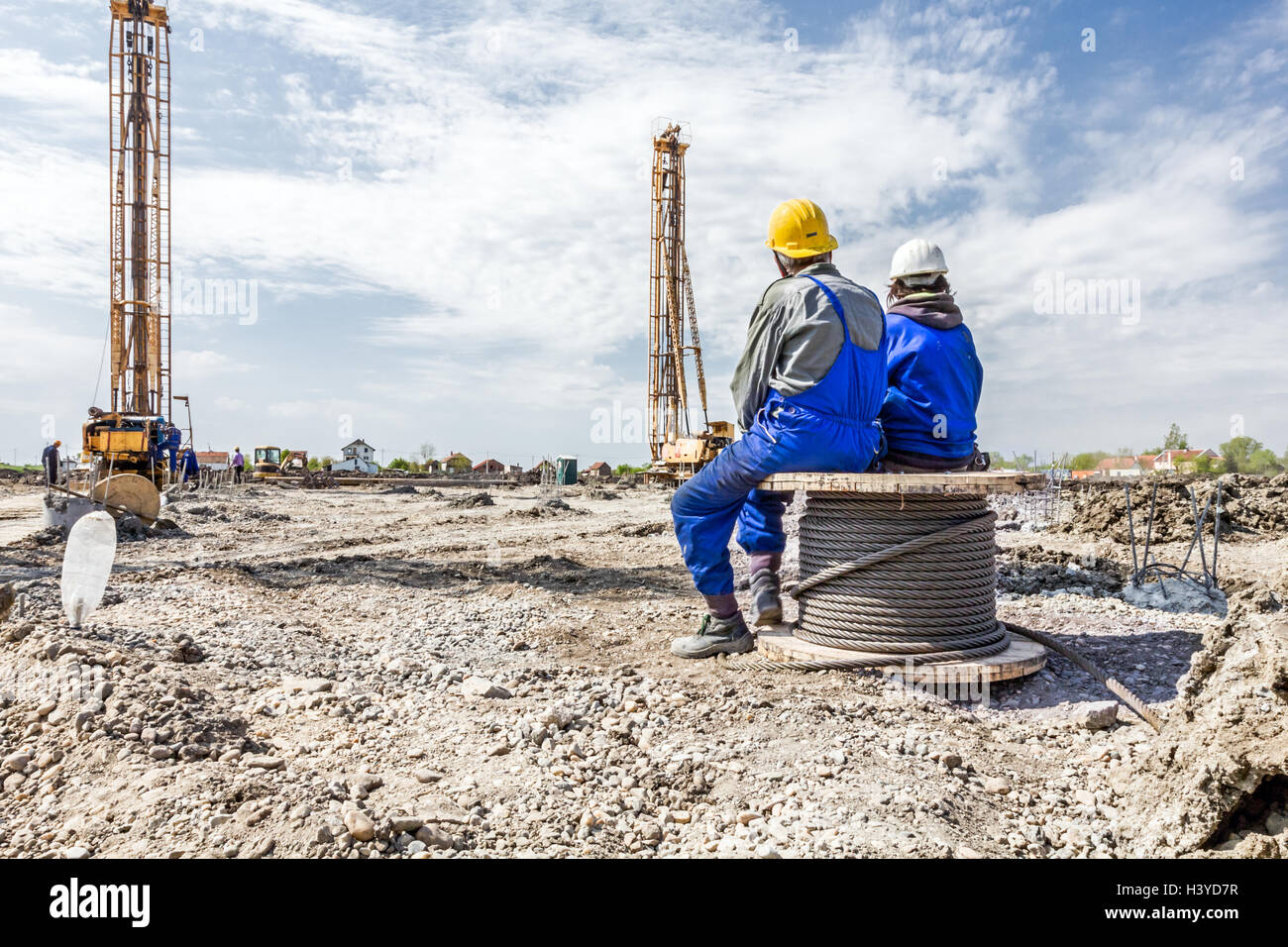 Two construction workers with helmets are sitting on wooden spool with ...
