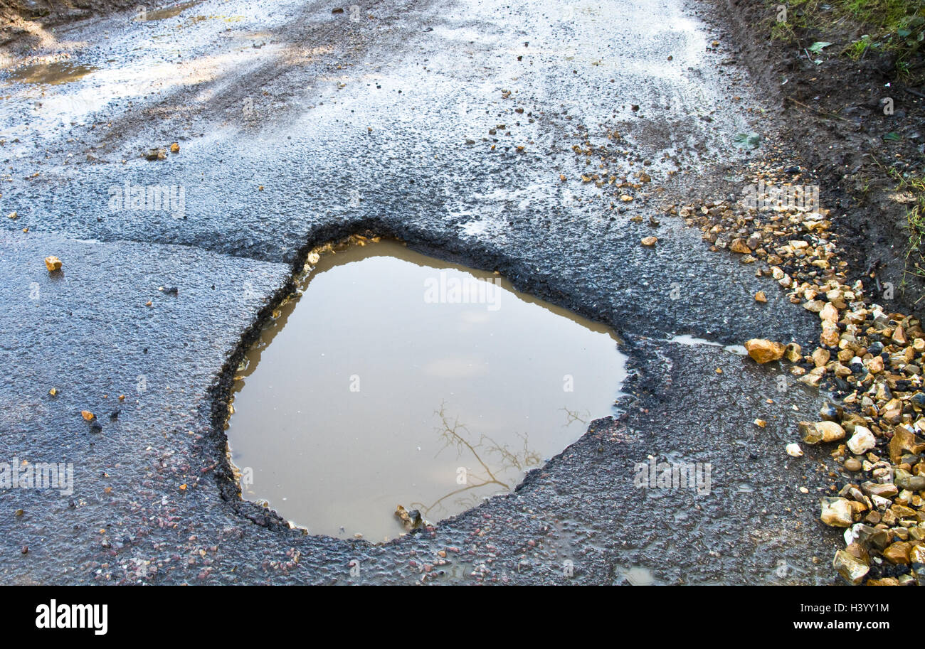 Severe winter damage to a tarmac road producing a large, deep ...