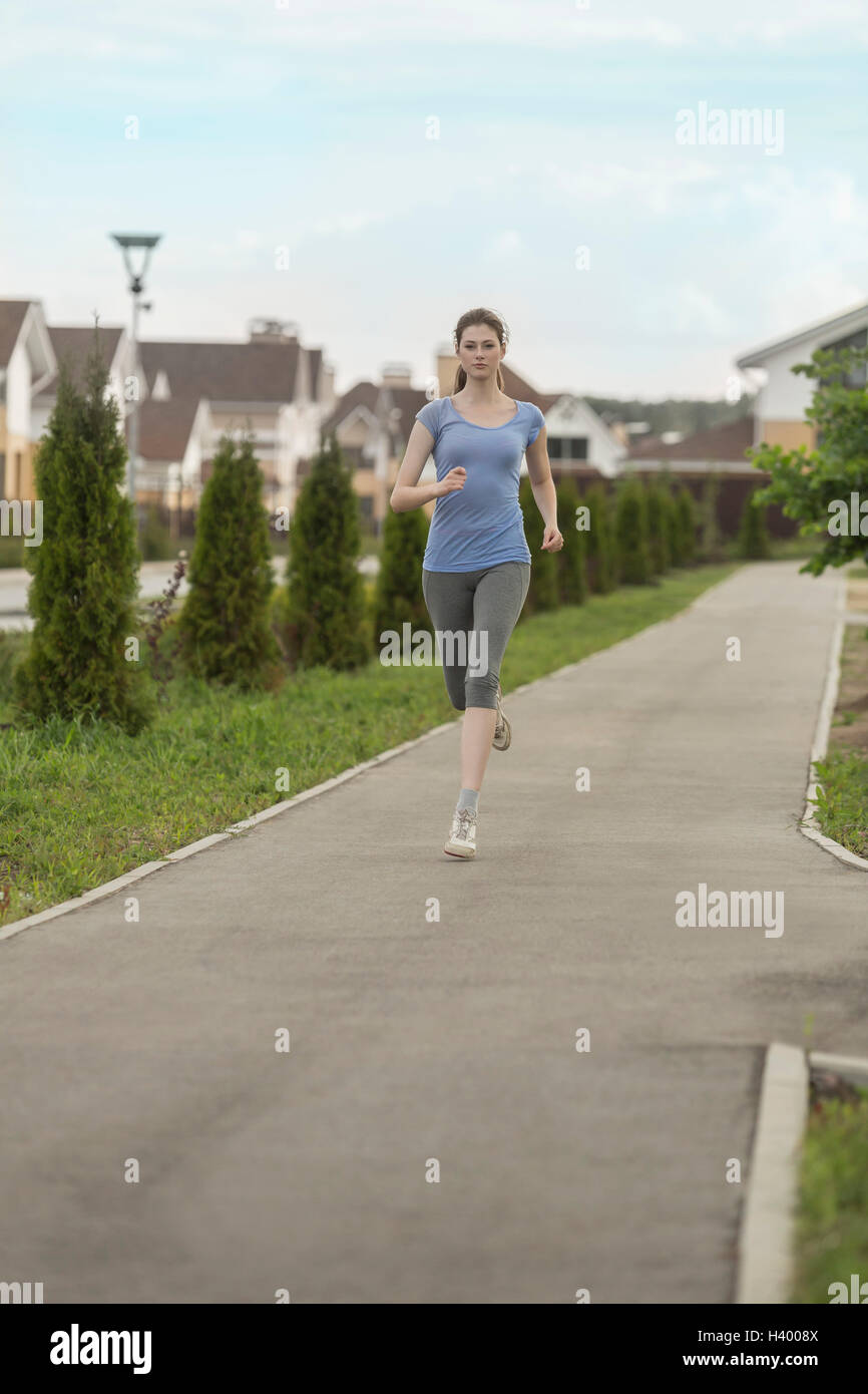 Young woman jogging on footpath by topiary in residential district ...