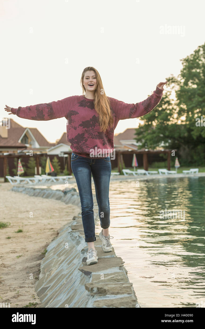 Woman with arms outstretched standing at lakeshore against clear sky ...
