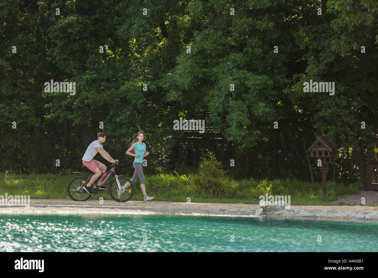 Woman jogging while man cycling by lake in park Stock Photo - Alamy