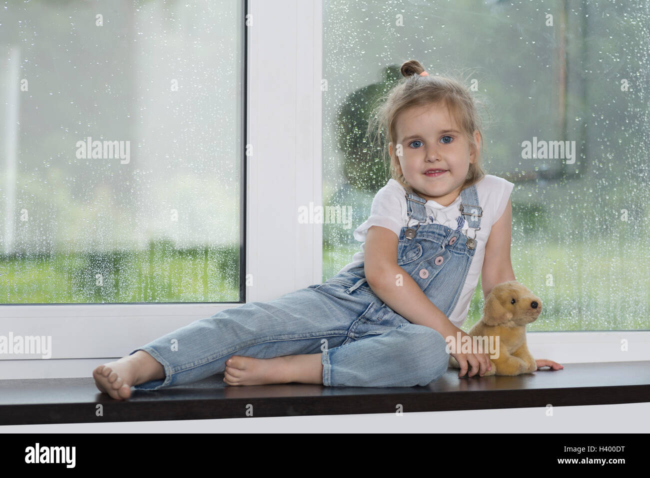 Portrait of cute smiling girl sitting with stuffed toy on window sill ...