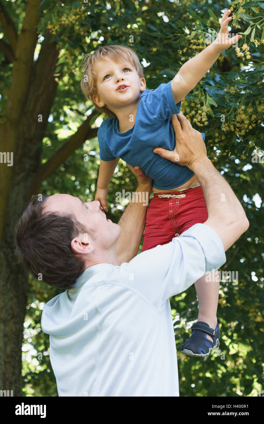 Low angle view of father lifting son against tree Stock Photo - Alamy