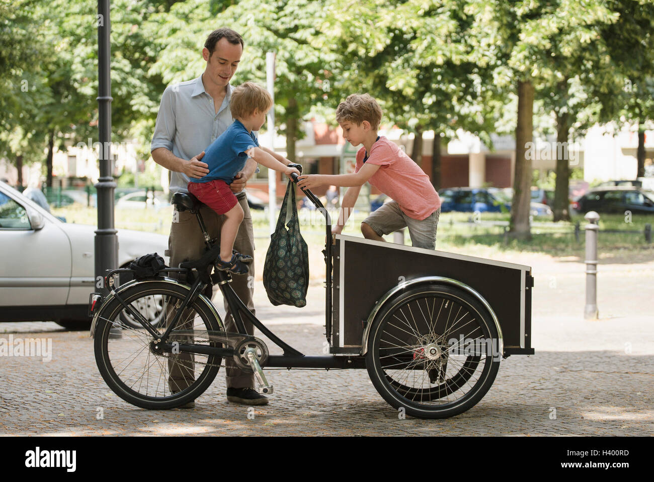 Boys playing on bicycle by father standing on street Stock Photo - Alamy