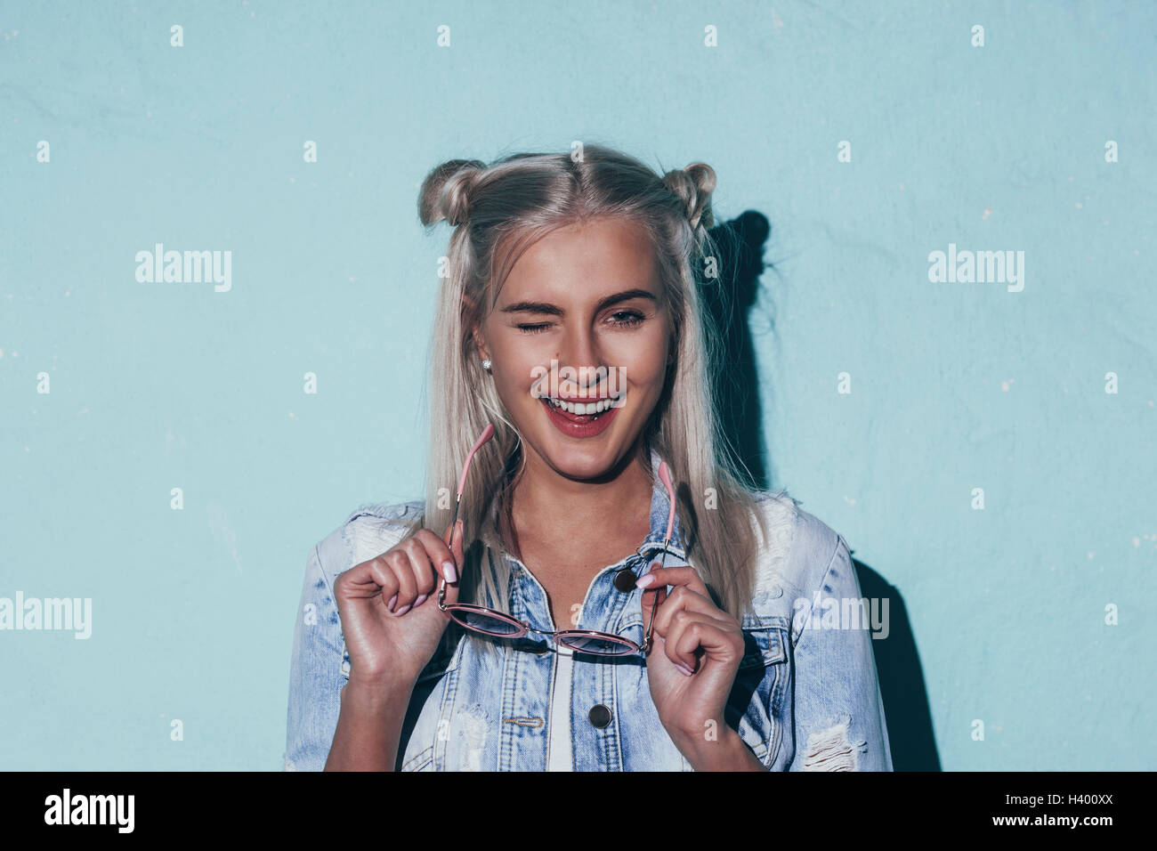 Portrait of beautiful young woman winking while holding sunglasses ...