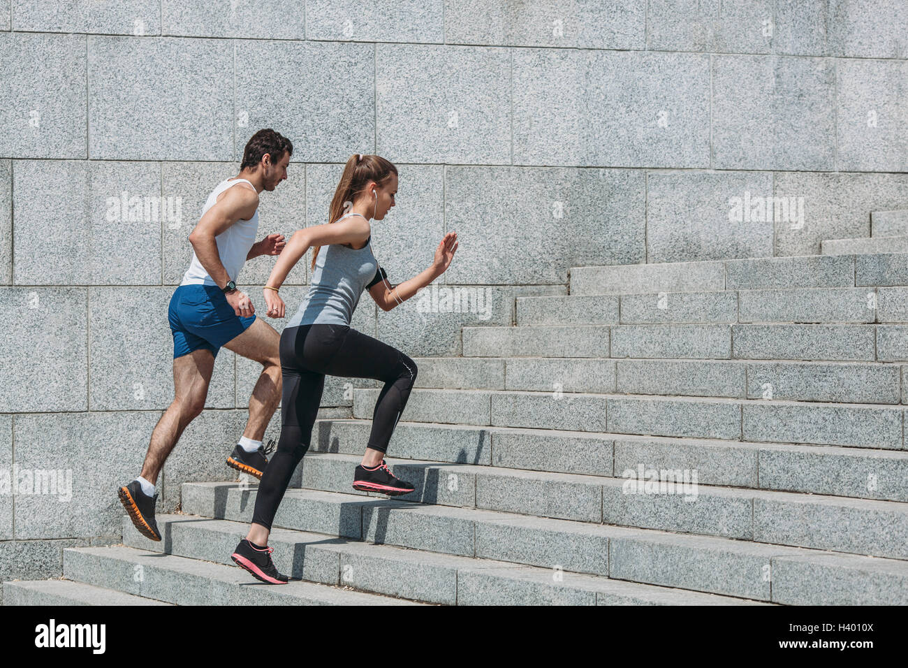 Determined friends jogging up steps by wall Stock Photo - Alamy