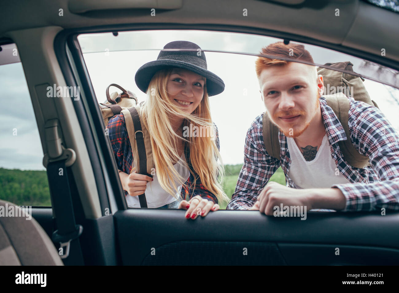 Smiling male and female backpackers looking into car window Stock Photo ...