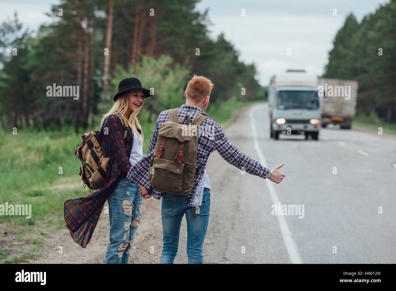 Happy couple hitchhiking on roadside at forest Stock Photo - Alamy