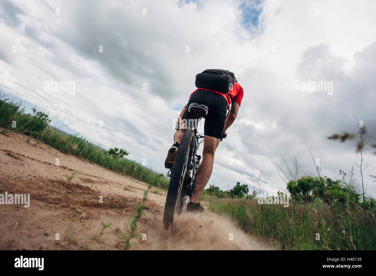 Low angle view of man riding mountain bike on dirt road against cloudy ...