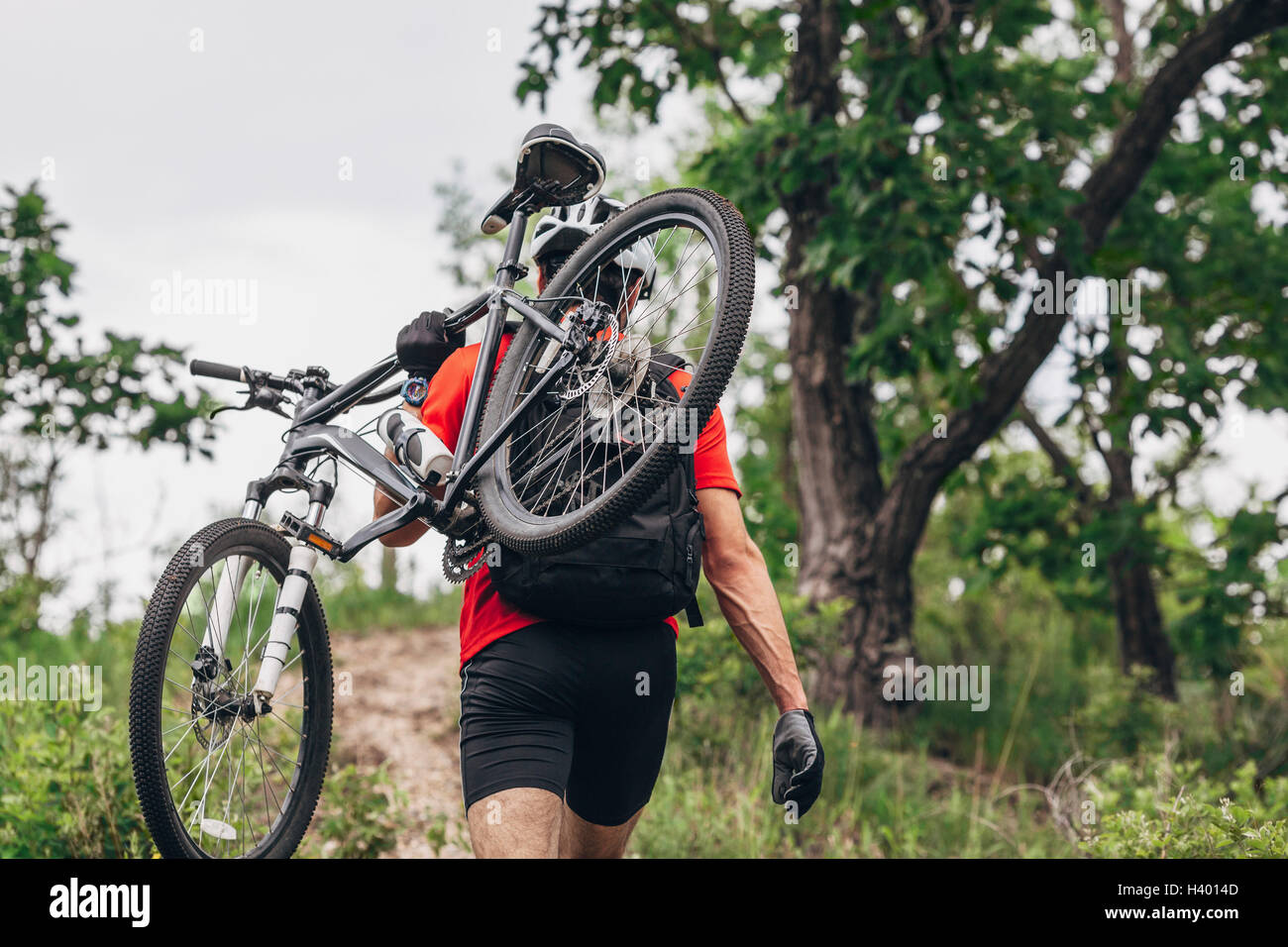Rear view of man carrying mountain bike up hill Stock Photo - Alamy