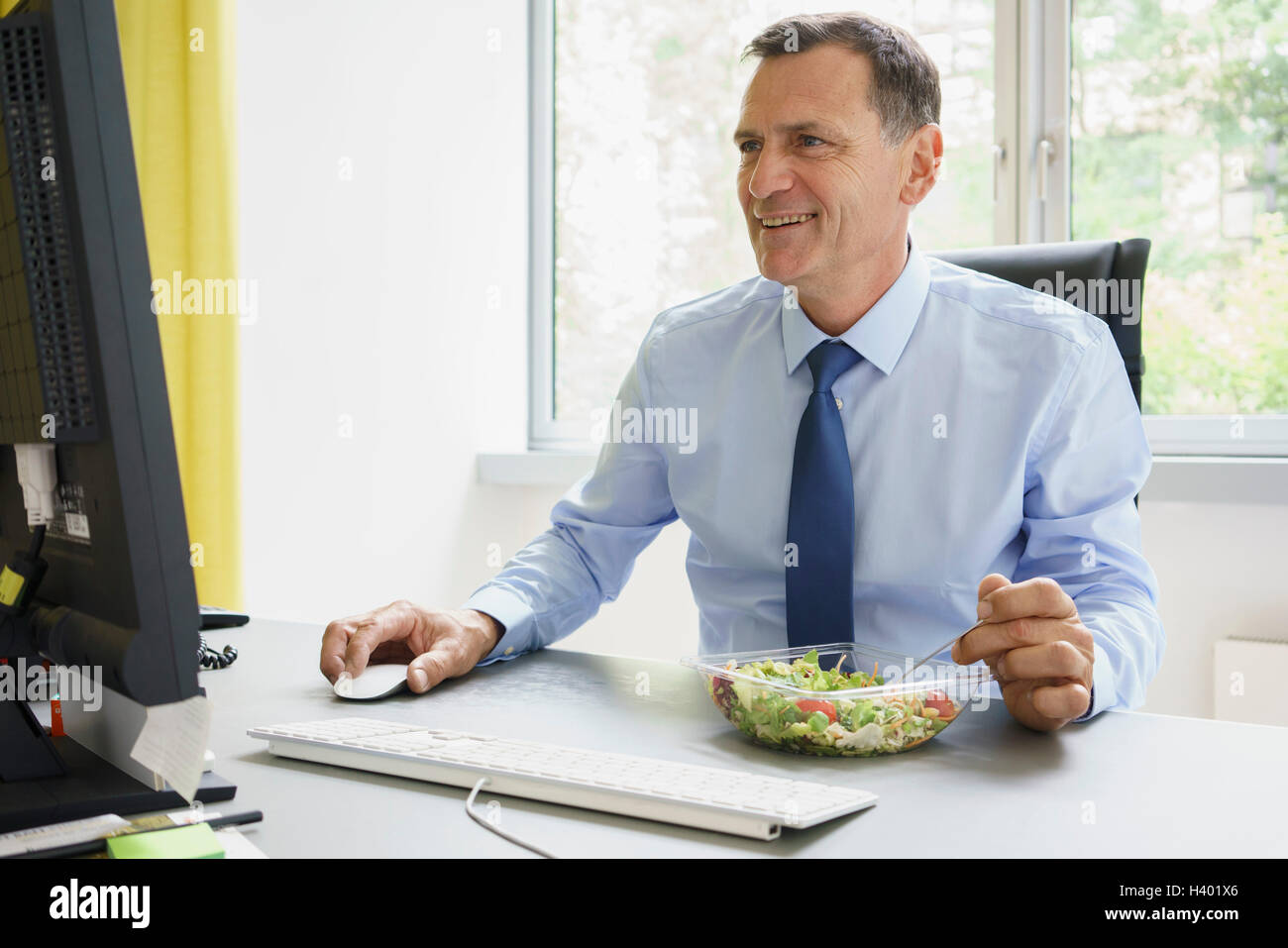 Smiling businessman working on computer while having salad at desk in ...