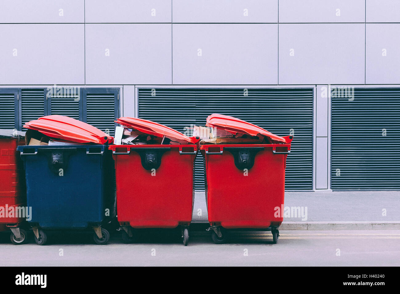 Red and blue garbage bins on roadside against wall Stock Photo - Alamy