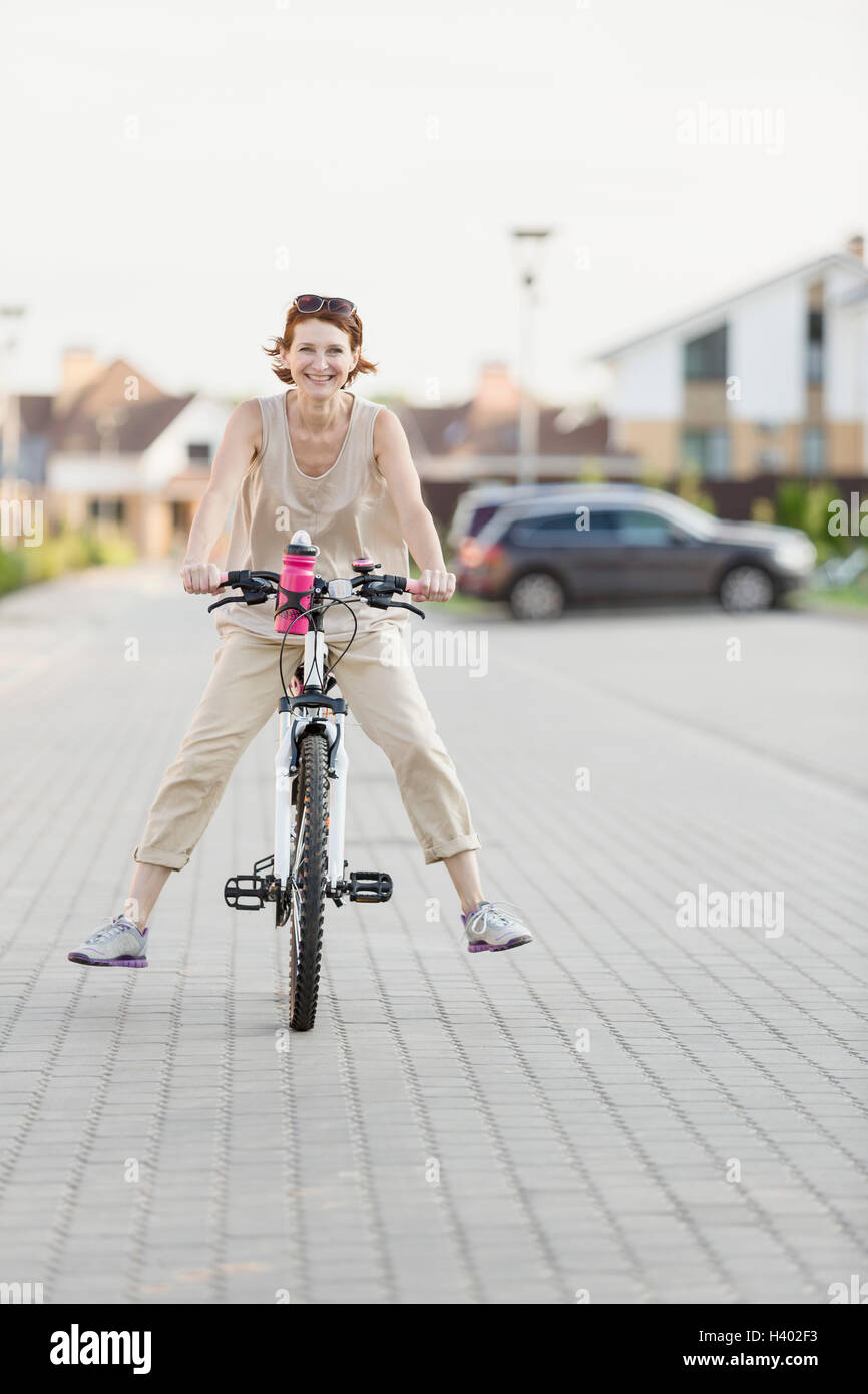 Portrait of happy woman riding bicycle on cobbled street Stock Photo ...