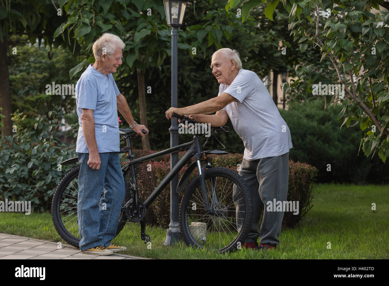 Smiling friends talking while standing by bicycle on field at park ...
