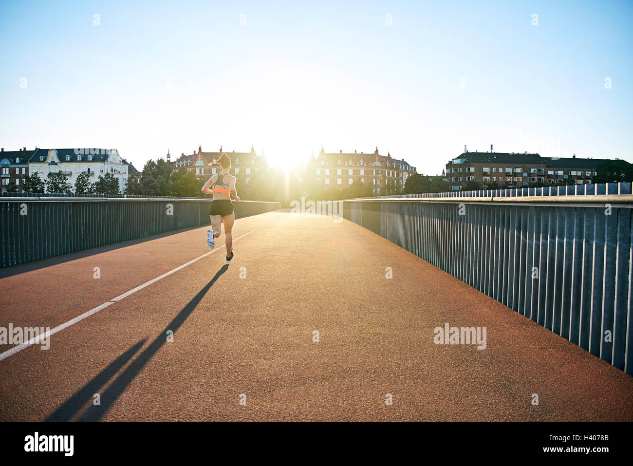 Rear view of single woman running down bridge with long shadow behind ...