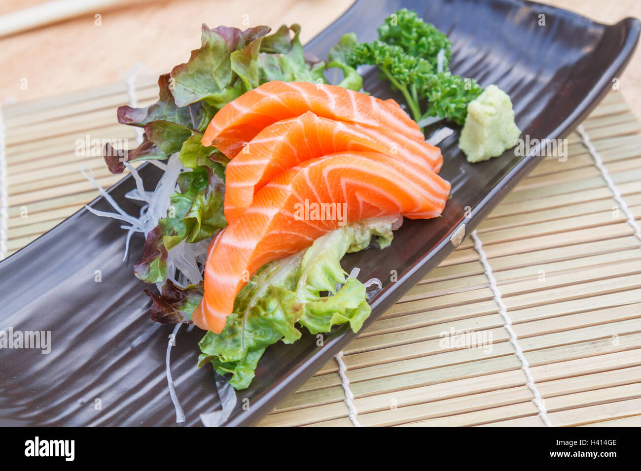 Sashimi salmon with vegetable and radish in black plate and chopsticks ...