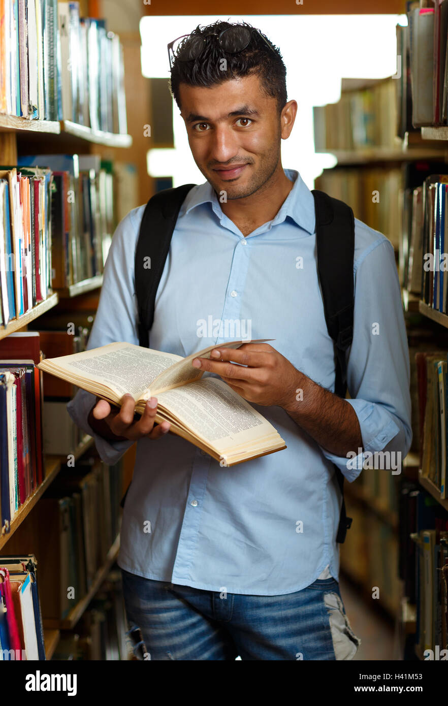 Young arab student reading book between the shelves in the library ...