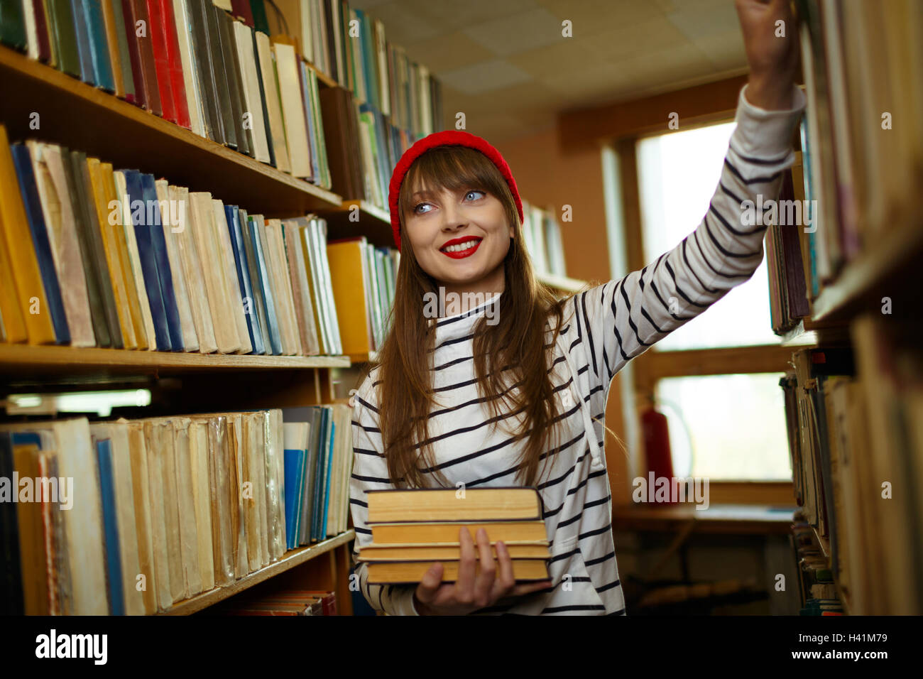 Young student girl choosing books between the shelves in the library ...