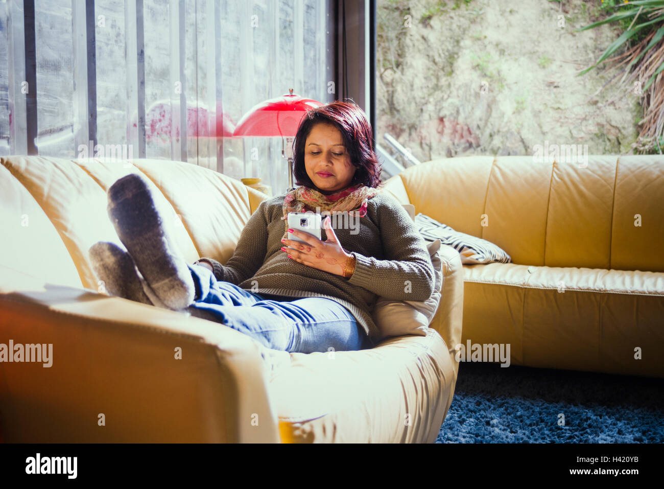 Woman sitting on sofa texting on cell phone Stock Photo - Alamy