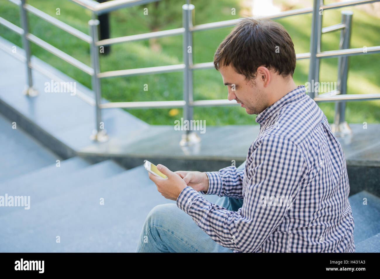 Man uses his Mobile smart Phone outdoor while sitting on a stairs ...