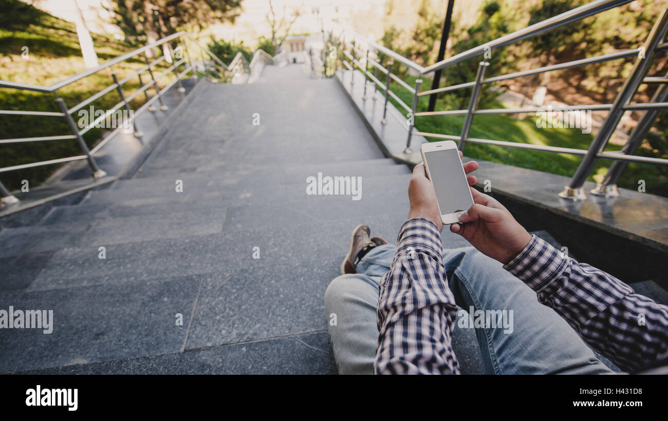 young Man with the phone in his hand sitting on the steps. top view ...