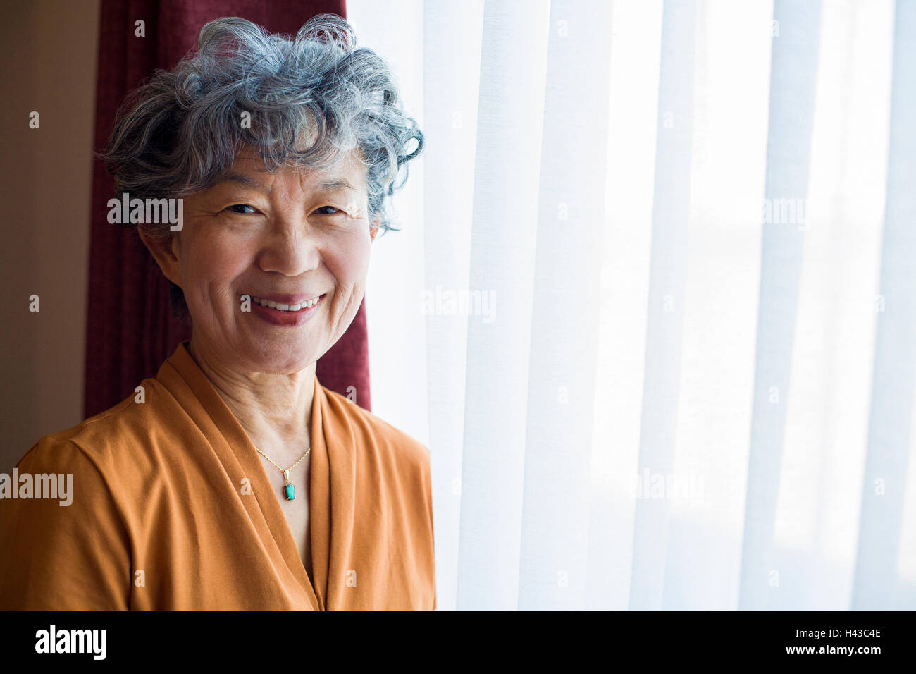 Smiling Japanese woman standing at window Stock Photo - Alamy