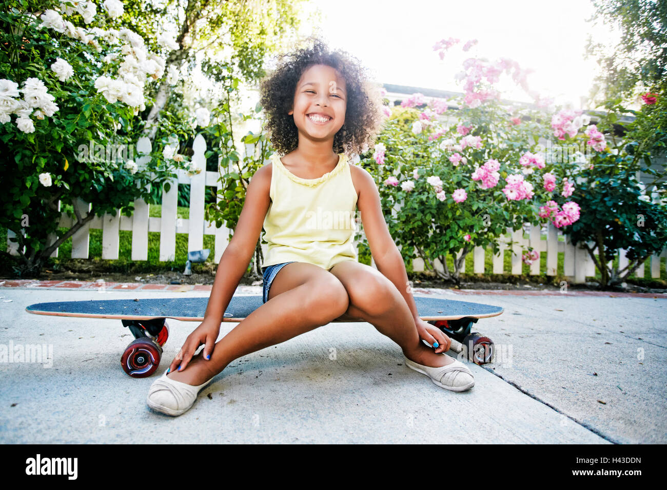 Smiling Mixed Race girl sitting on skateboard Stock Photo - Alamy