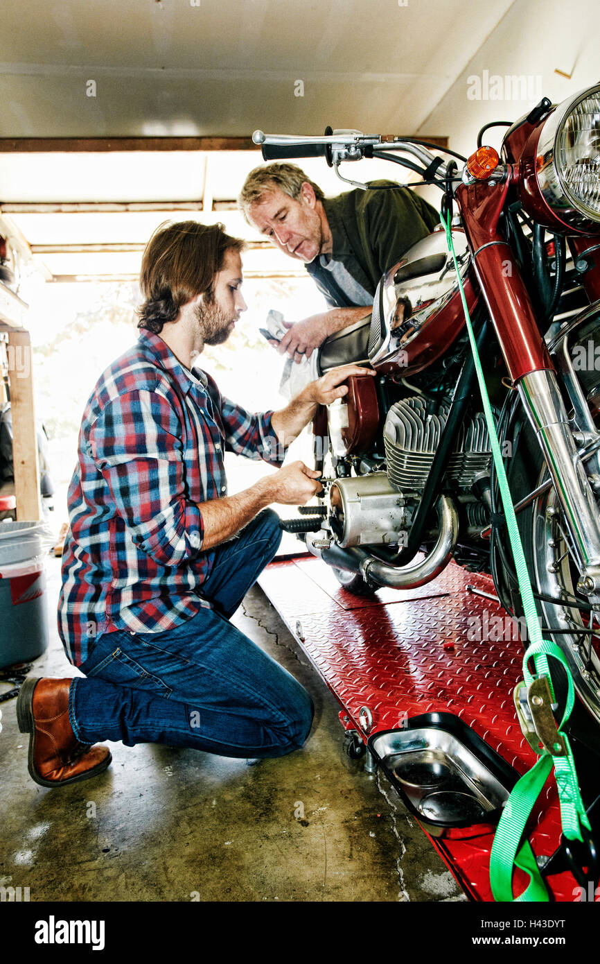 Caucasian father watching son repairing motorcycle in garage Stock ...