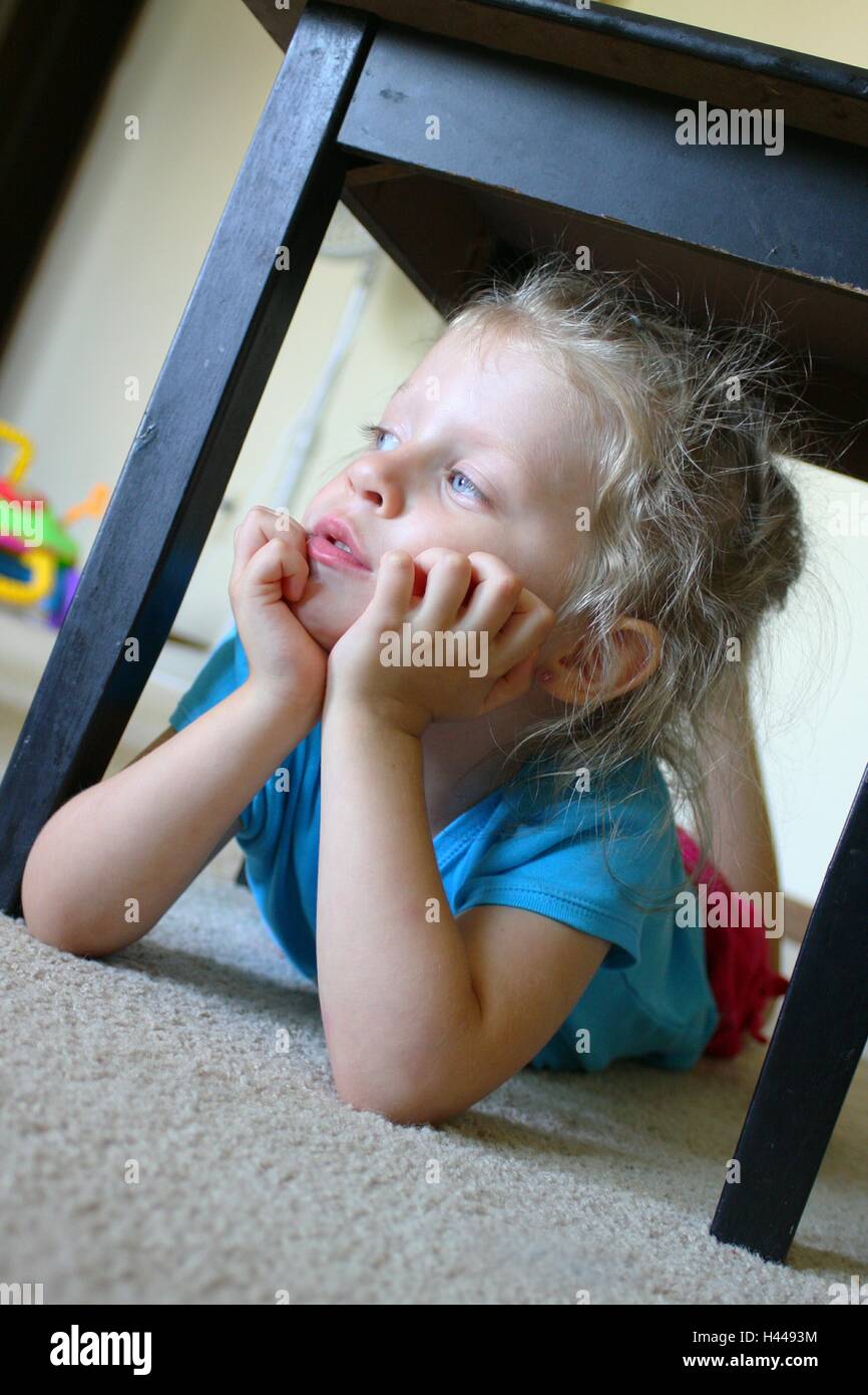 young child or girl hiding under a small table gazing out of the window ...