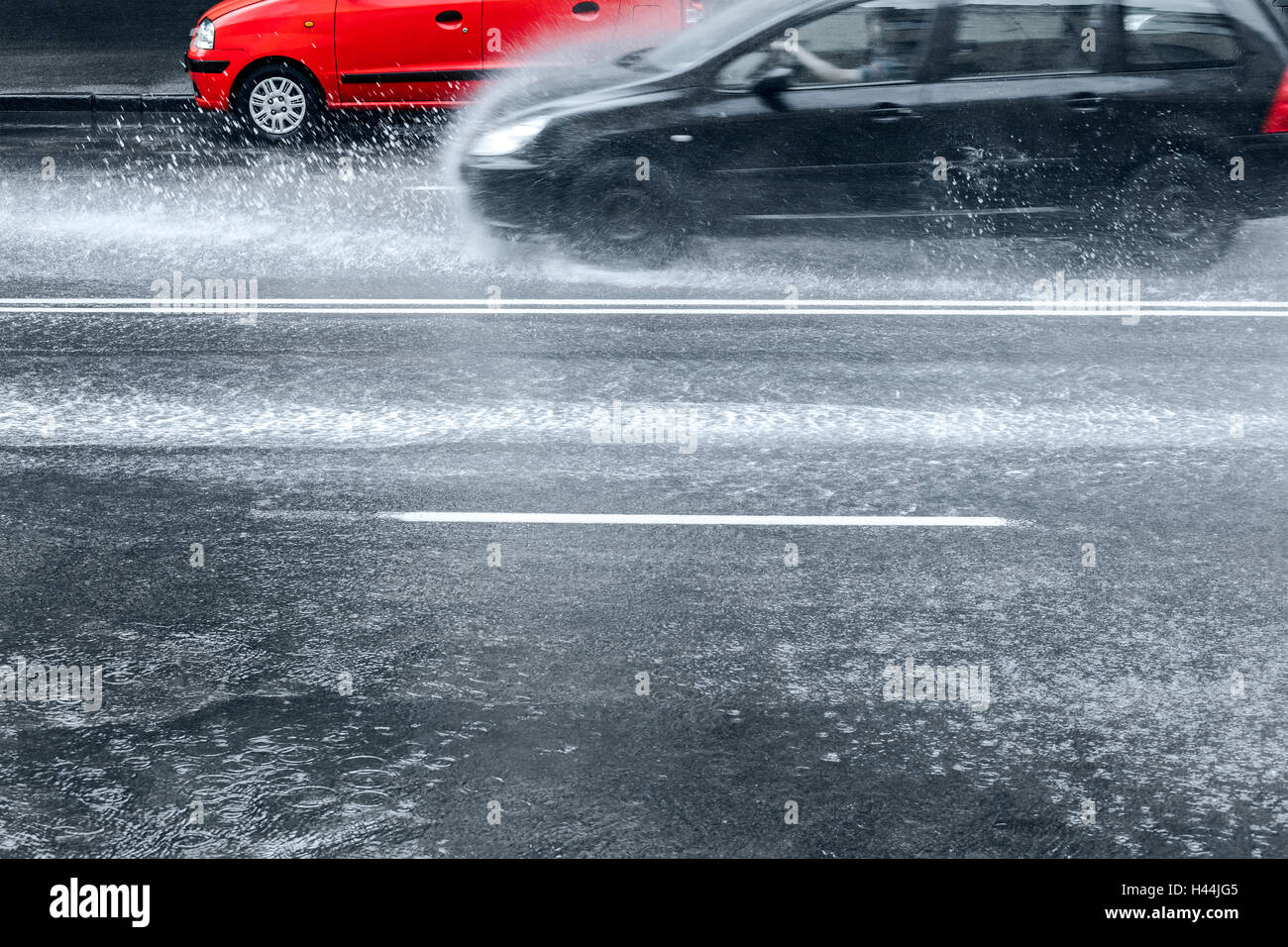 cars driving through water puddles on city road with water spraying ...