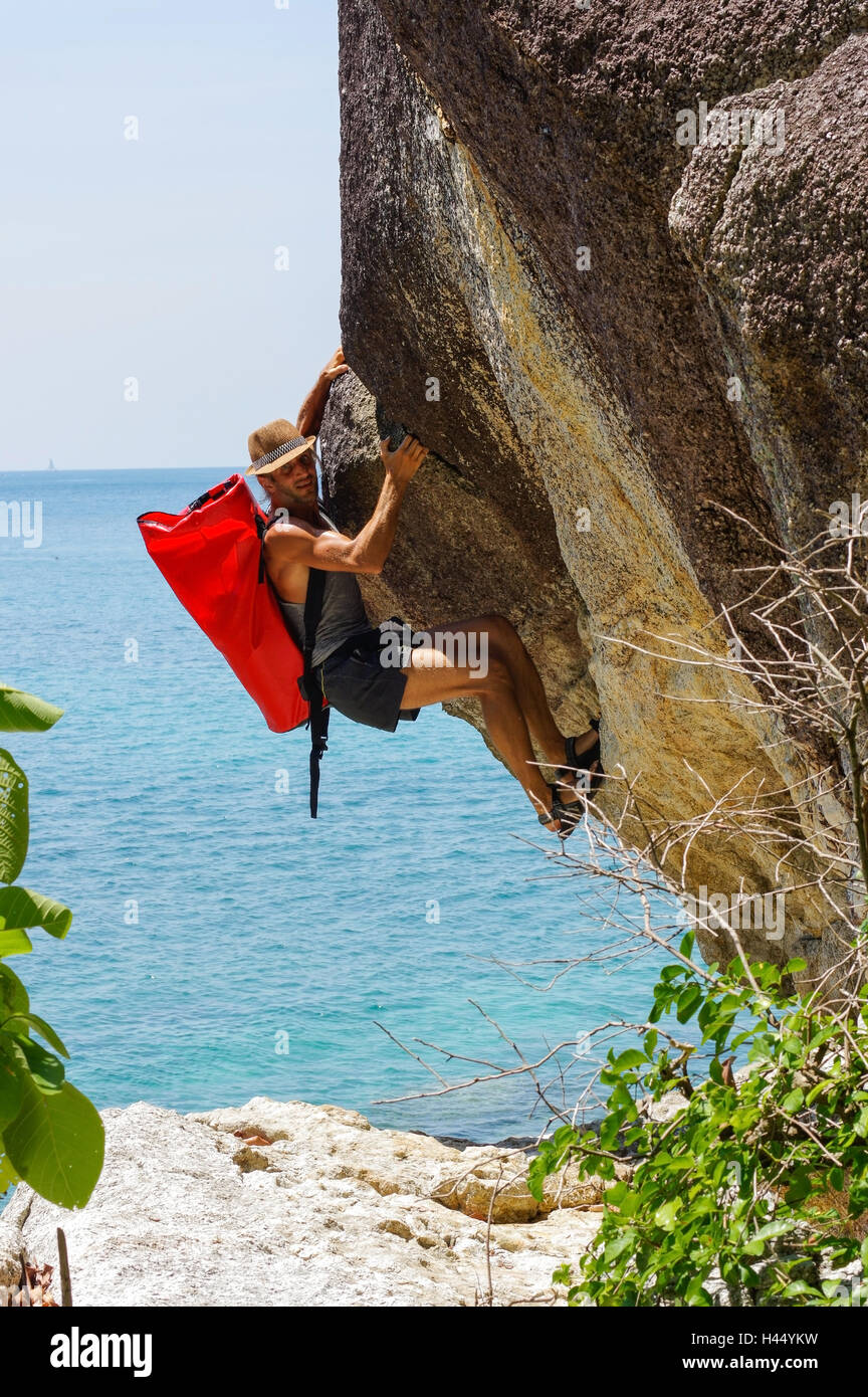 a strong and happy man climbing on high rock over the sea with a hut ...