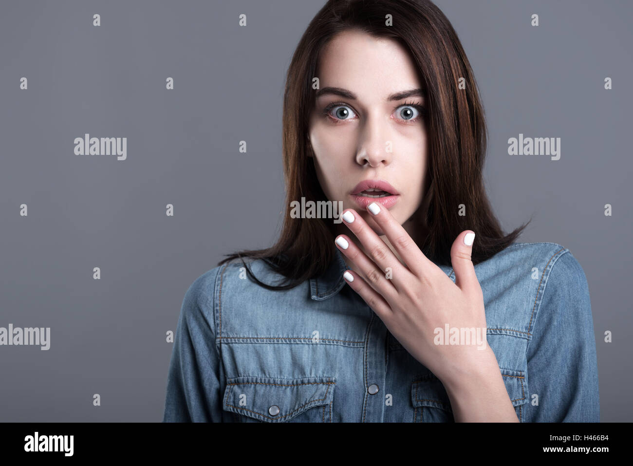 Scared young woman raising hand to her mouth Stock Photo - Alamy