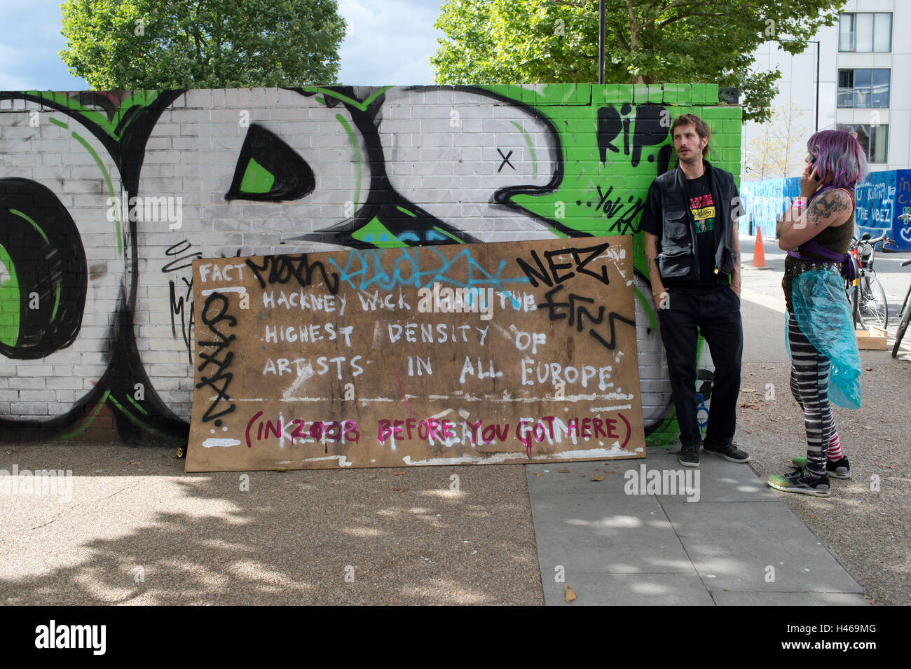 A young man and woman stand next to a notice about art and Hackney Wick ...