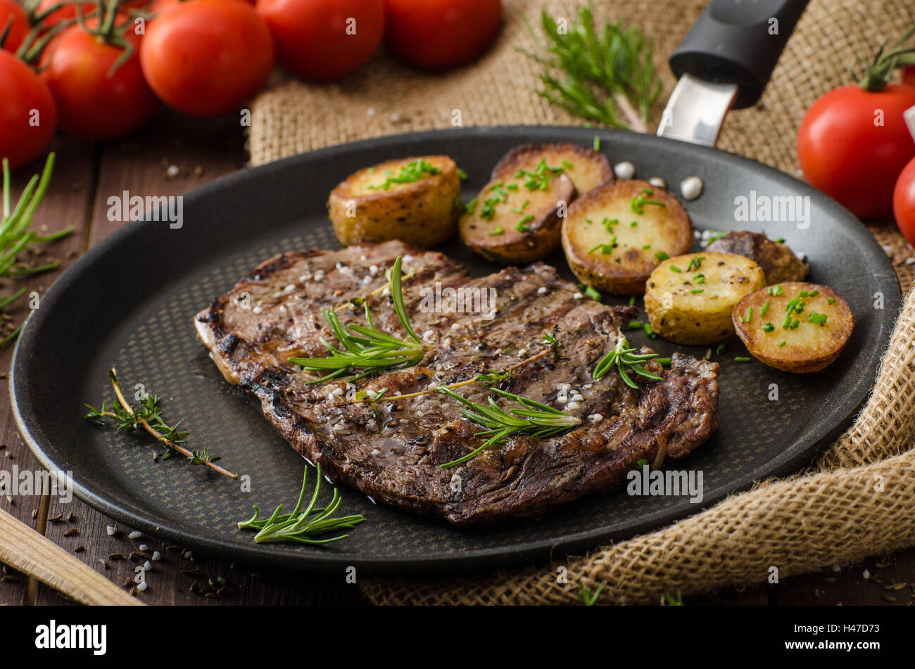 Beef rib eye steak with rustic potatoes, fresh herbs and tomatoes ...