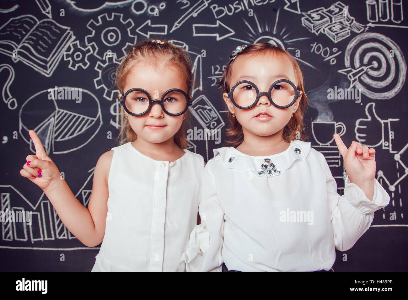 Two little smart girls in glasses lifting finger up on a background of ...