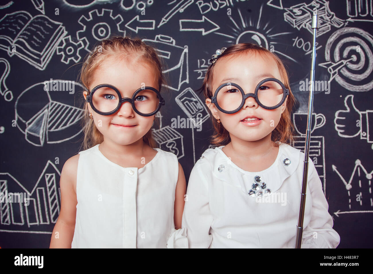 Two little smart girls in glasses holding a pointer on dark background ...