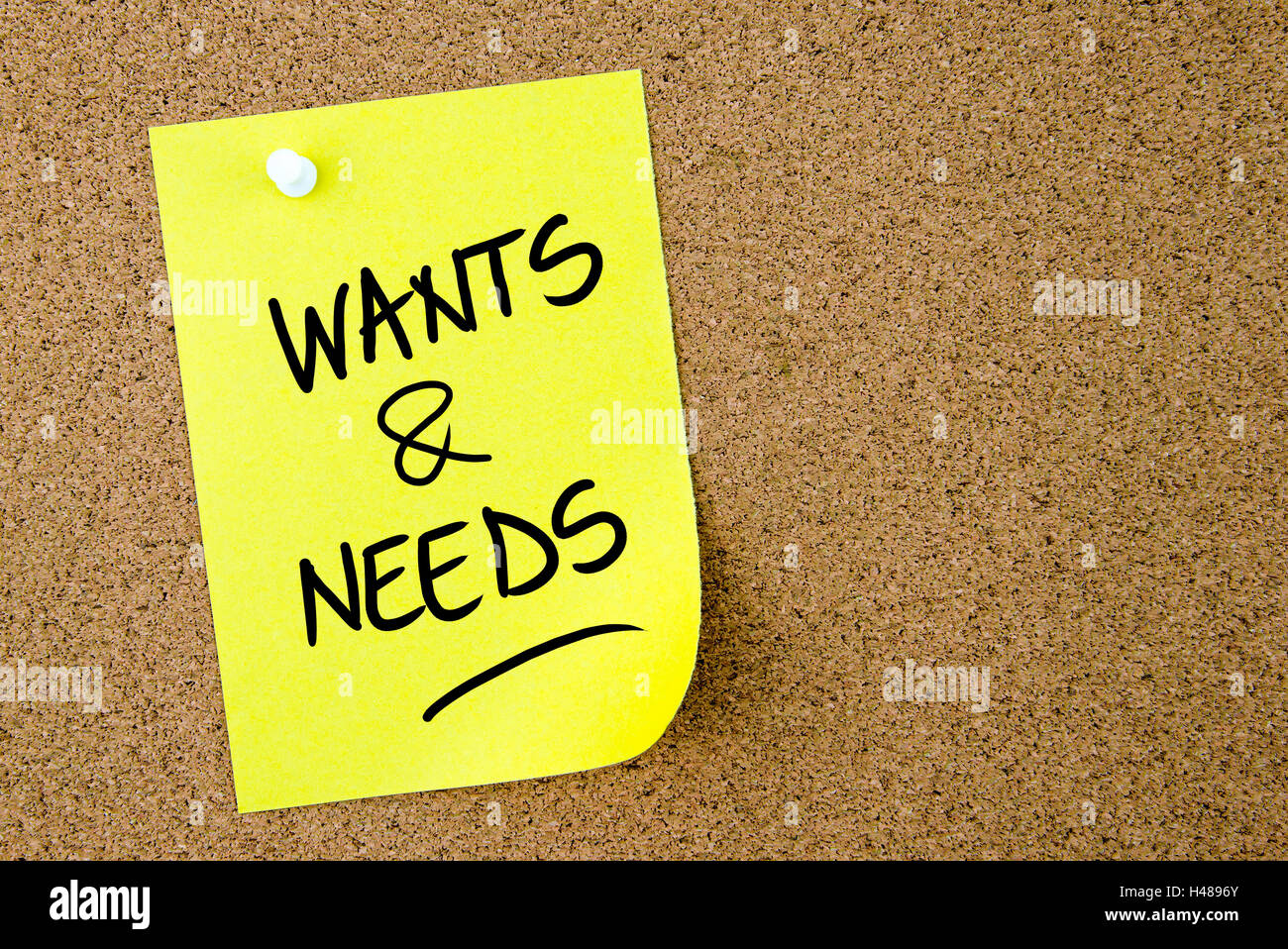 Wants and Needs text written on yellow paper note pinned on cork board ...