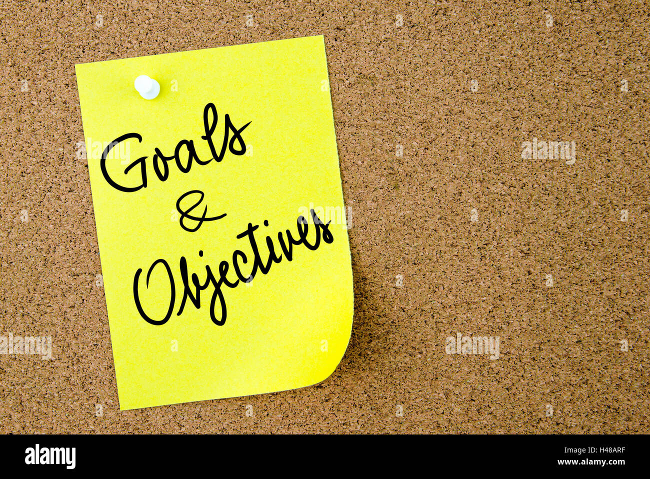 Goals and Objectives text written on yellow paper note pinned on cork ...