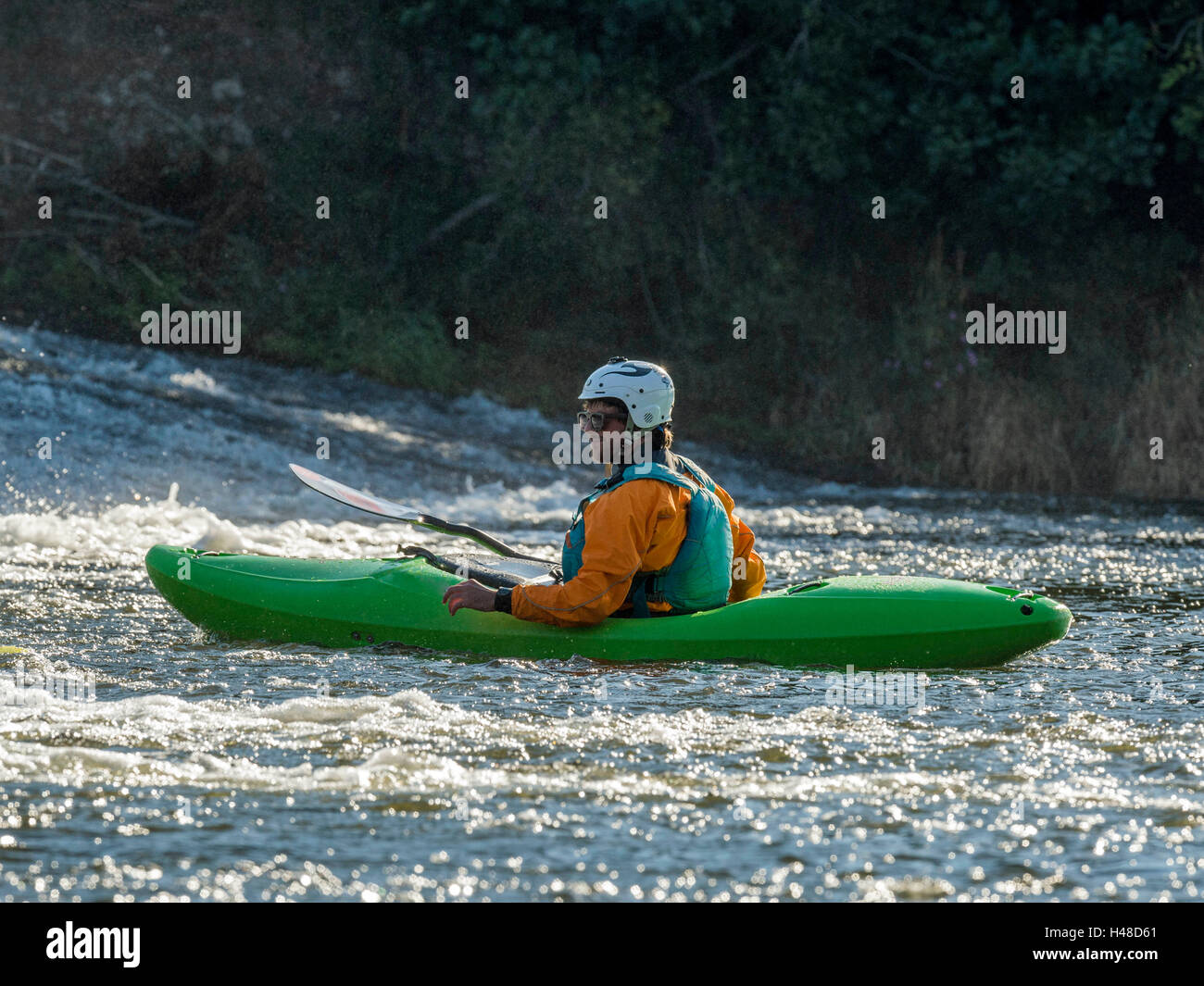 Male adult White Water Kayaking along a River Exe Weir on a bright ...