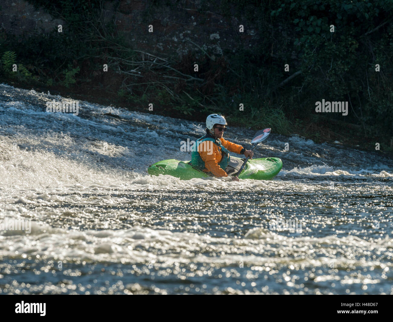 Male adult White Water Kayaking along a River Exe Weir on a bright ...