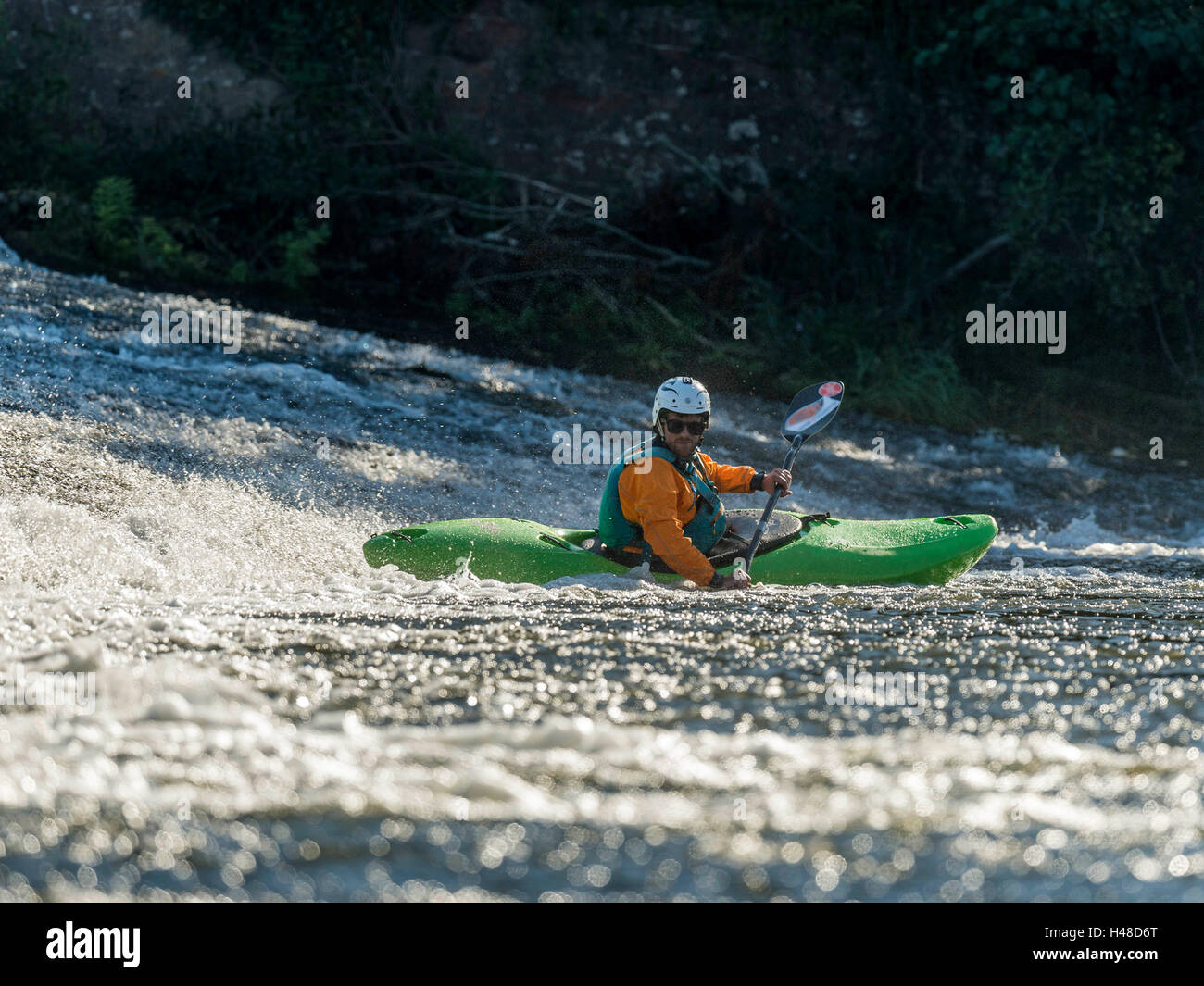 Male adult White Water Kayaking along a River Exe Weir on a bright ...