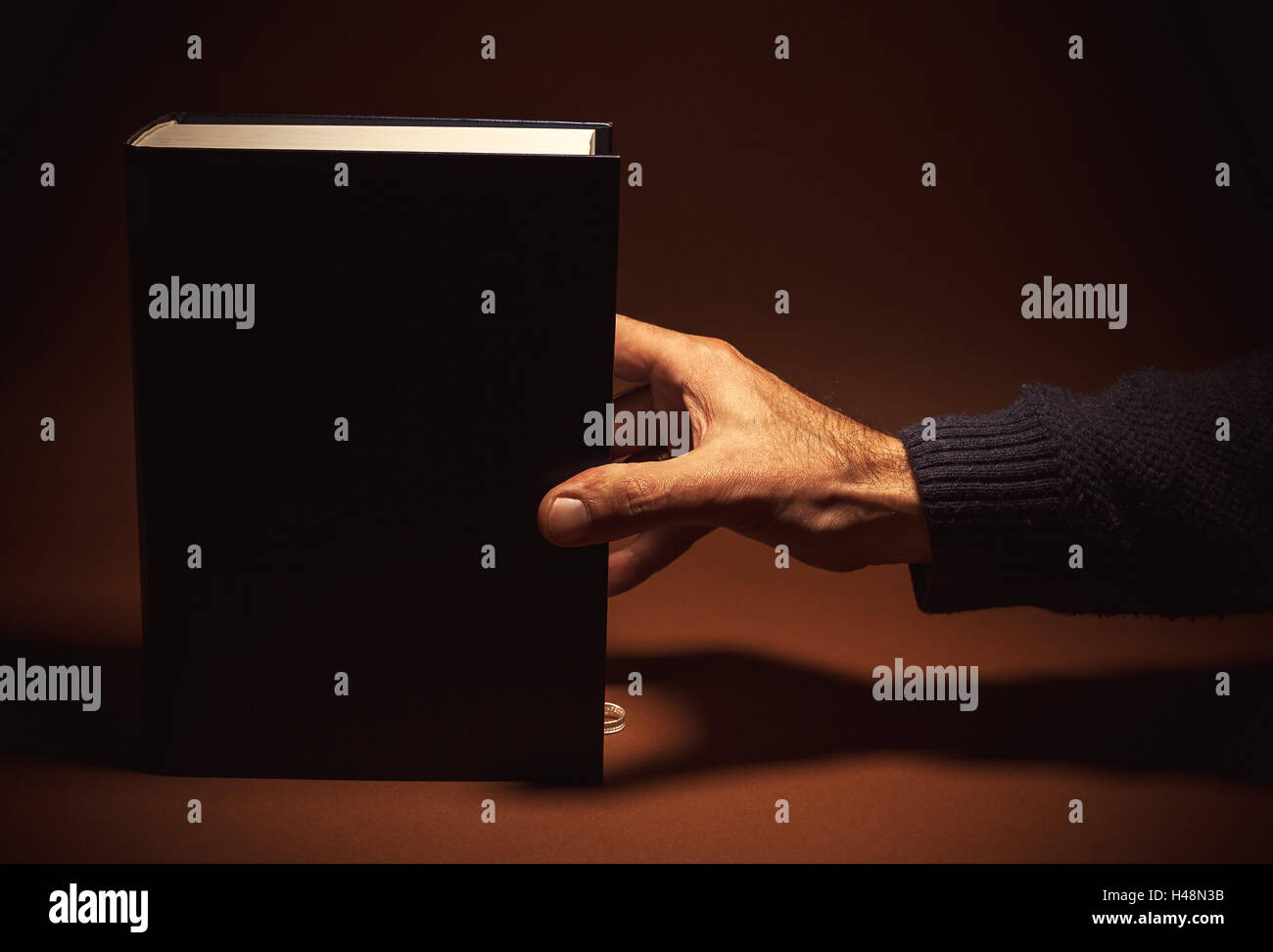 One thick book in a male hand, on brown background. Looks like ...