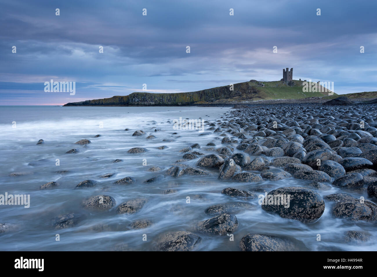 Dunstanburgh Castle above the boulder covered Embleton Bay ...