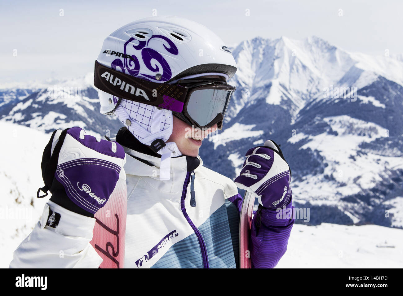 Girl standing with skis in front of mountain landscape, smiling, side ...