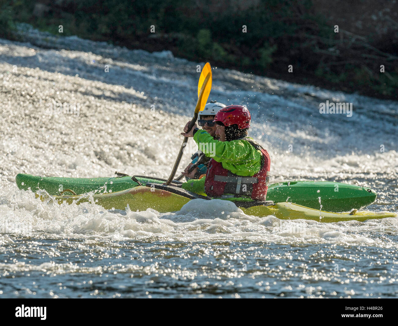 Two male adults White Water Kayaking along a River Exe Weir on a bright ...