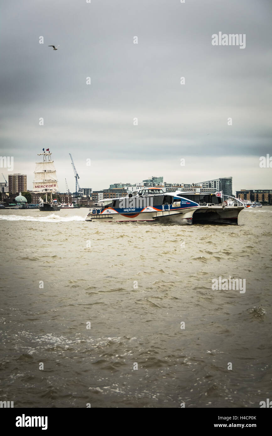 A Thames Clipper hydrofoil and a Tall Ship pass each other on grey and ...