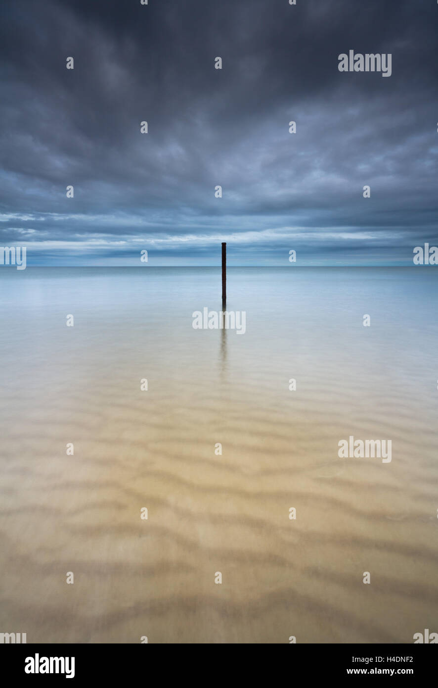 Single metal post in the golden sand at high tide, North sea under a ...