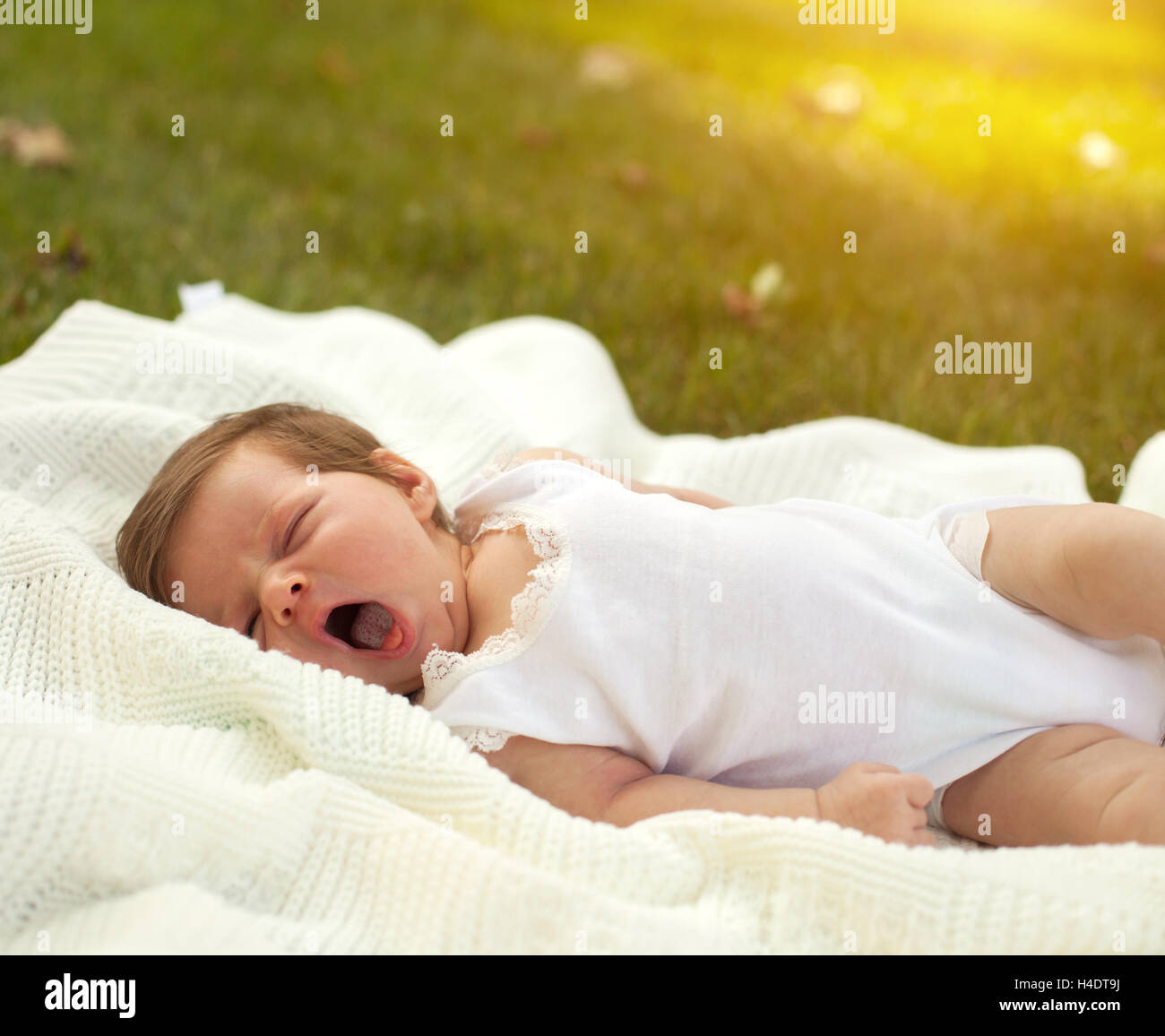 Baby yawing on the blanket on the grass Stock Photo - Alamy