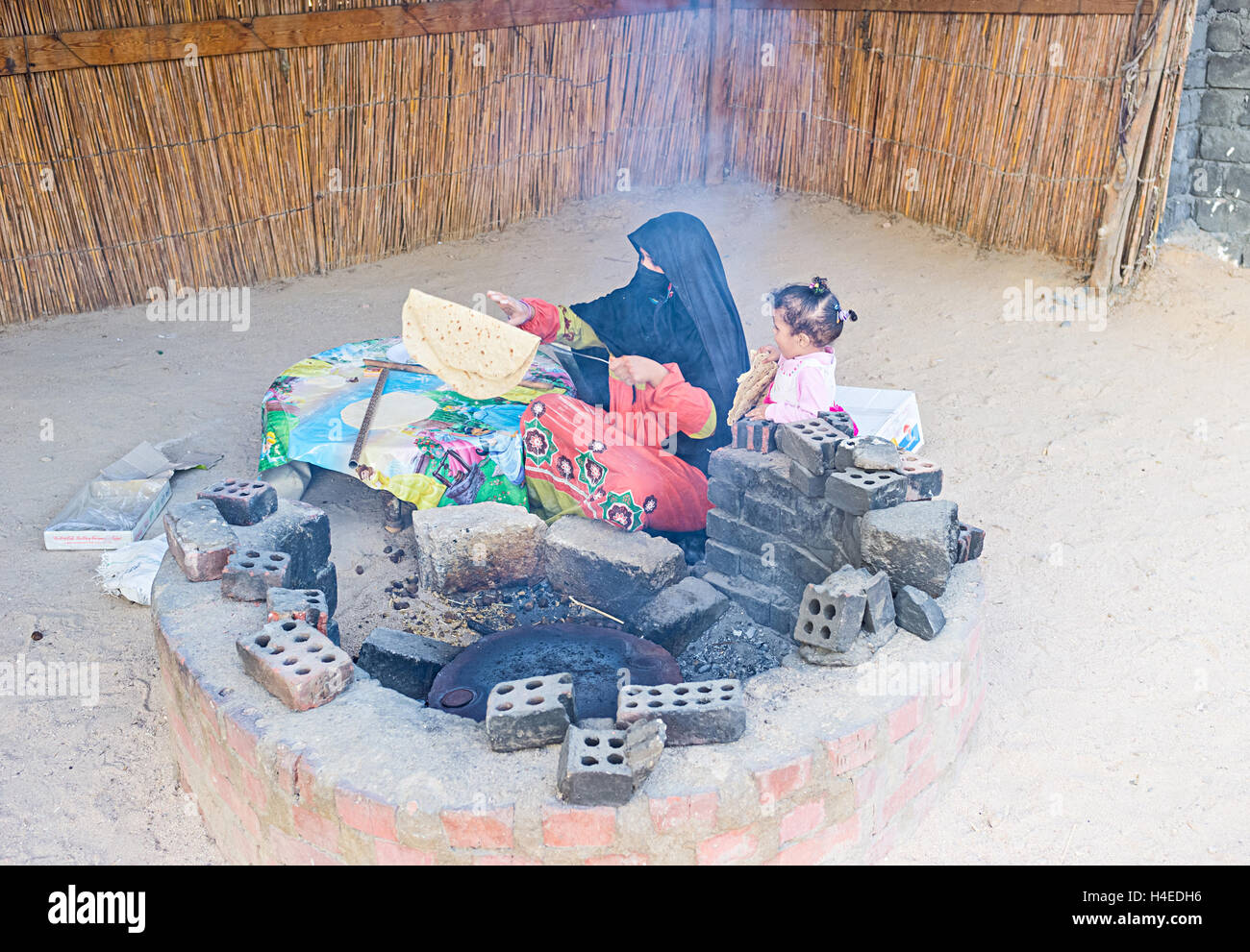 The Bedouin woman cooks the bread in the outdoor oven, sitting on the ...