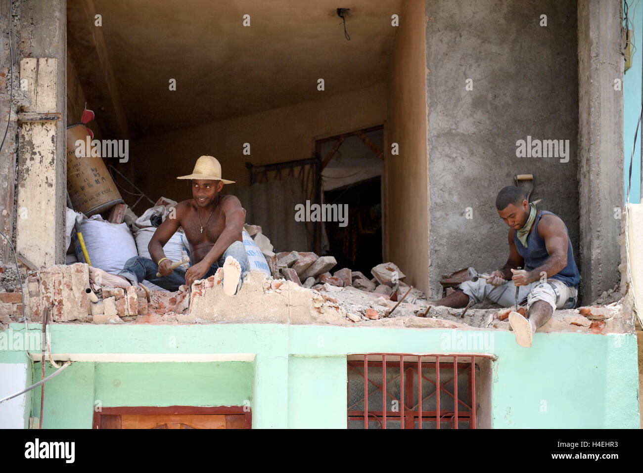 Two builders doing building works in a house; building's front wall is ...